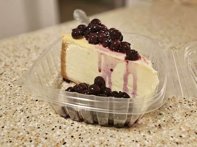 Cheesecake crowned with blueberry royalty—where New York tradition meets Florida's sweet tooth in a plastic container of pure joy.