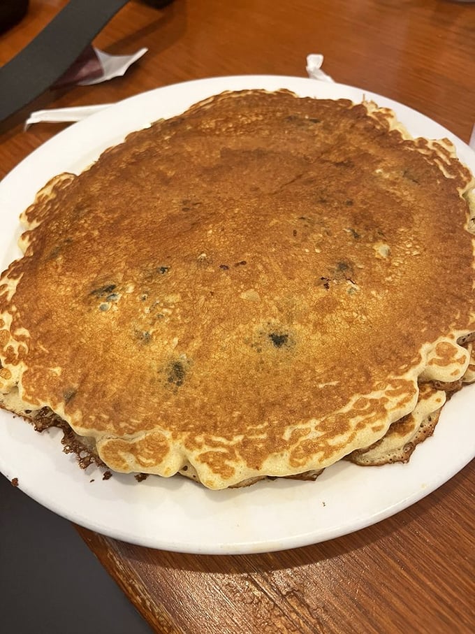 This pancake isn't just big—it's the size of your childhood dreams, perfectly golden and studded with blueberries like edible sapphires.