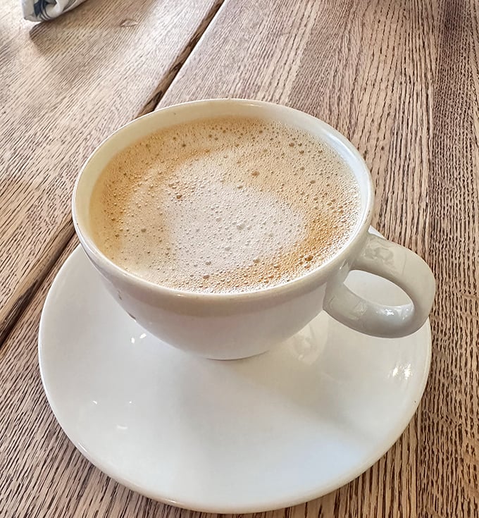 A proper cappuccino served in white porcelain against weathered wood – the morning ritual that separates "just waking up" from "actually being awake."