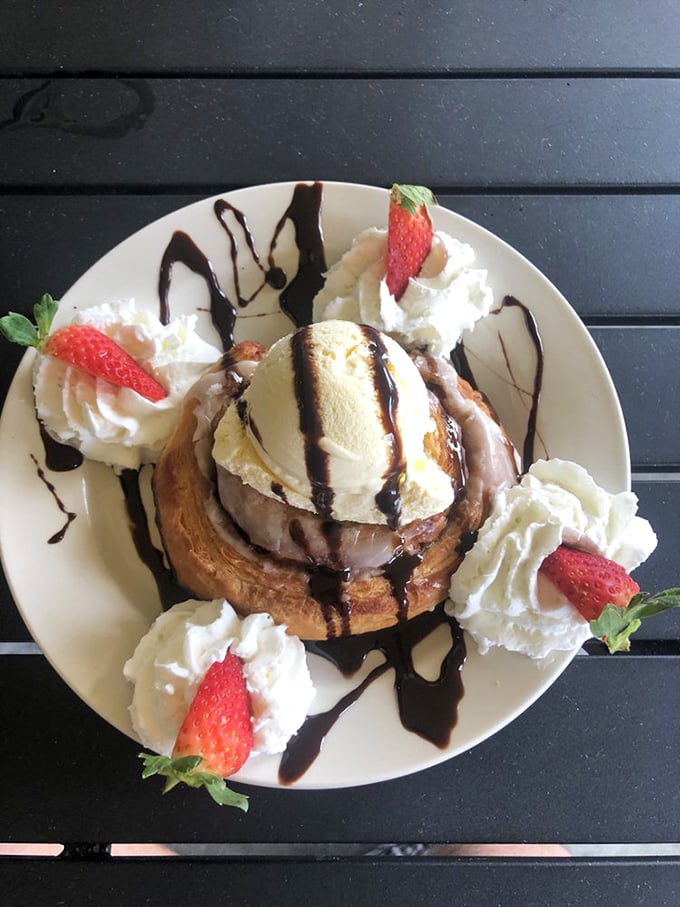 When your cinnamon roll arrives looking like dessert for breakfast, complete with strawberries and theatrical chocolate drizzle presentation.