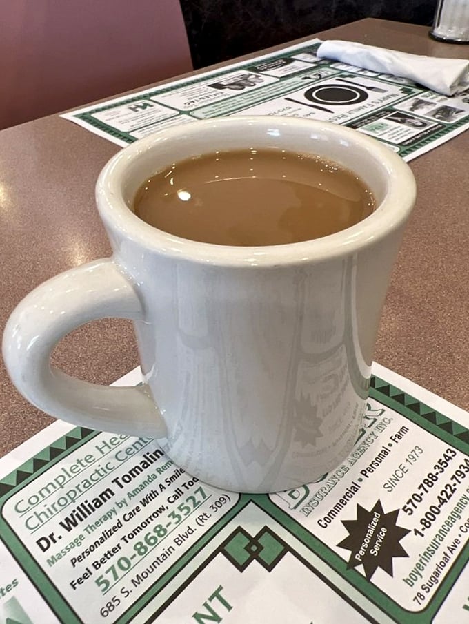 The sturdy white mug – diner coffee's natural habitat – promising warmth, caffeine, and unlimited refills for road-weary travelers.