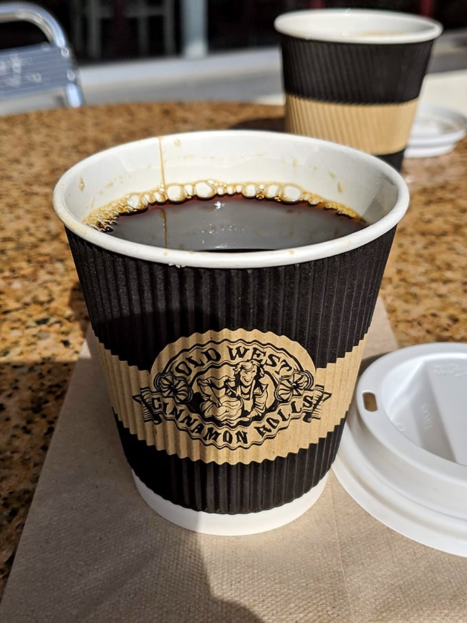 Coffee in its proper habitat—beside a cinnamon roll. The cup sleeve doubles as a reminder of where to return tomorrow morning.