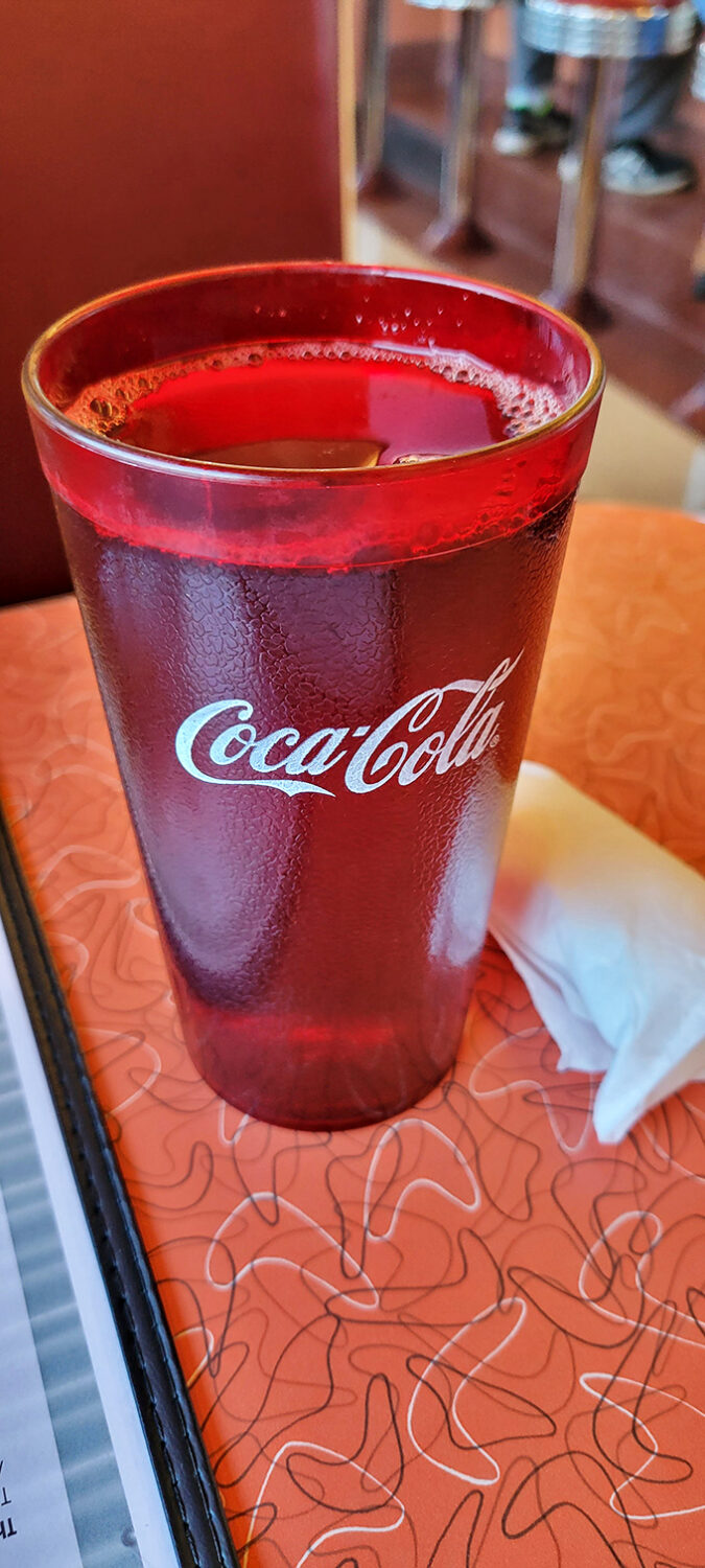 That classic Coca-Cola in a retro glass isn't just a drink—it's liquid nostalgia that somehow makes everything on your plate taste even better.