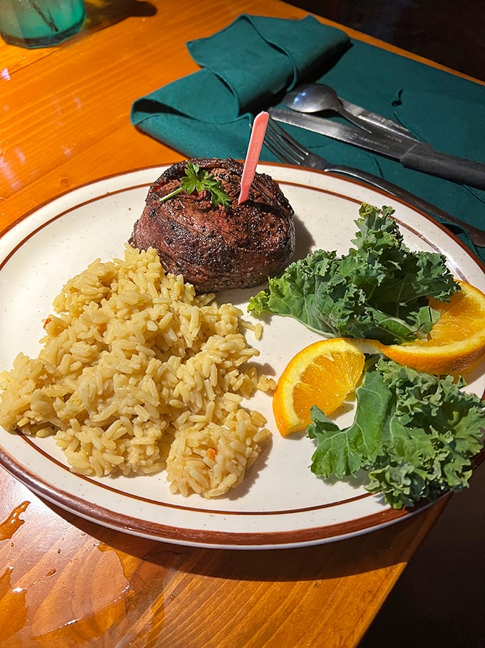 The filet mignon arrives like royalty with its rice pilaf courtiers and kale-orange garnish guards. The pink temperature marker is merely a formality.