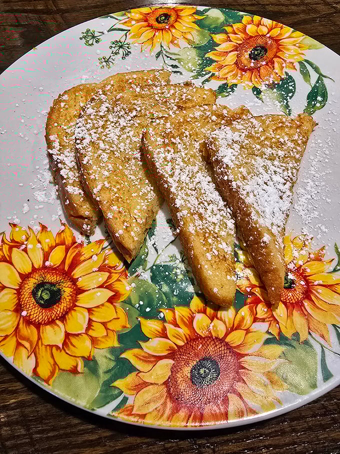 French toast dusted with powdered sugar on a sunflower plate—breakfast that makes you feel like you're eating at grandma's house, if grandma were a culinary genius.