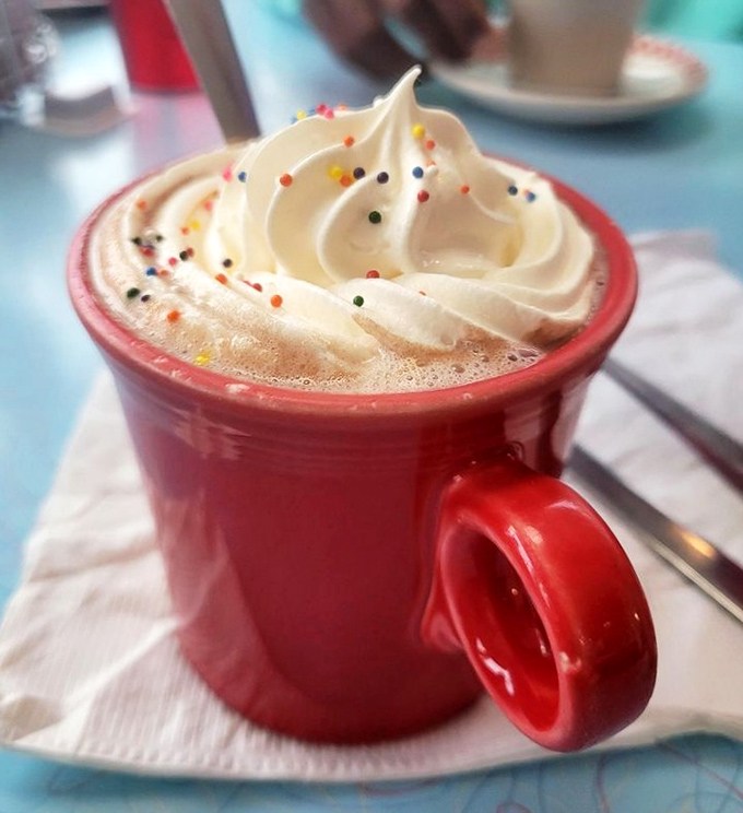 Hot chocolate that doesn't just arrive – it makes an entrance, topped with a cloud of whipped cream and sprinkles of childhood joy.