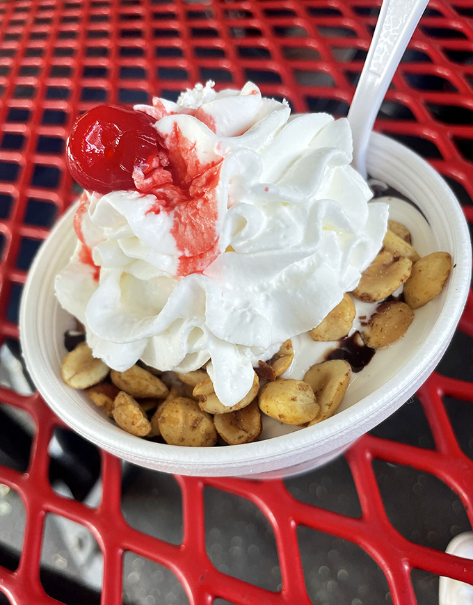 This sundae isn't just dessert—it's architecture. Whipped cream mountains, cherry summit, and a foundation of peanuts supporting the sweet skyscraper.
