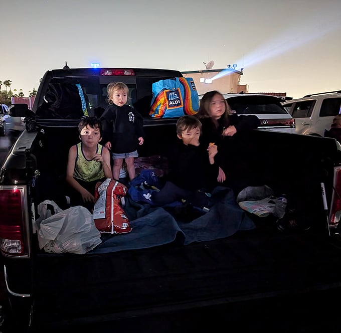 Family movie night reimagined—kids claiming territory in pickup beds with blankets and snacks, creating memories that'll outlast any streaming subscription.