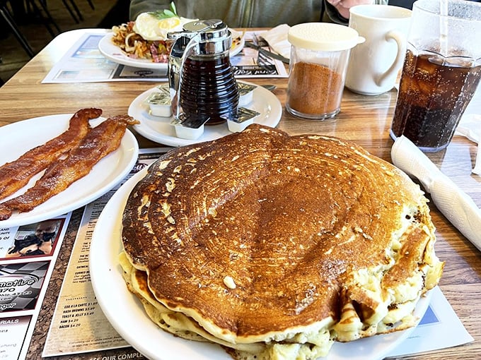 This pancake isn't just large – it's the size of your childhood dreams. The side of bacon is there for moral support.