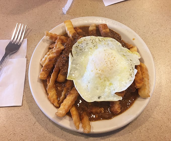 Fries swimming in chili with a sunny-side-up egg floating like a delicious life raft. Breakfast, lunch, and dinner having a party on one plate.