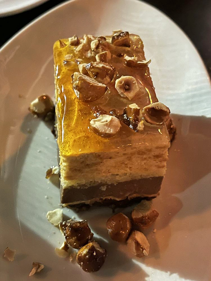 Dessert architecture at its finest – layers of flavor topped with what appears to be edible sunshine and hazelnut confetti.