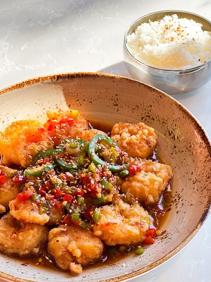 Crispy shrimp bathed in vibrant sauce with a scatter of fresh chilies – proof that sometimes the most beautiful things in life come with a little heat.