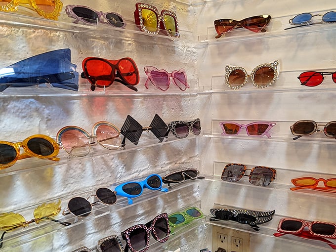Sunglasses from every era line lucite shelves—from Jackie O classics to Elton John spectaculars, each pair waiting for its next adventure.