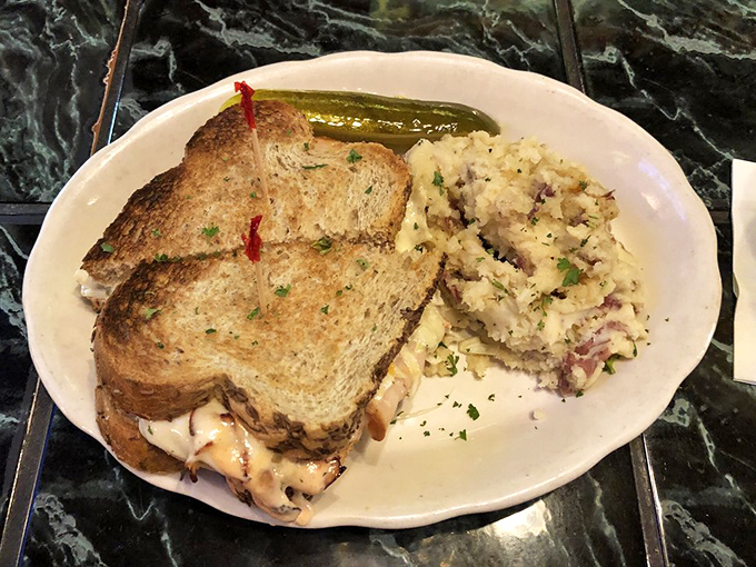 A sandwich that demands to be photographed before eaten – melty cheese cascading over toasted bread with that pickle spear standing guard.