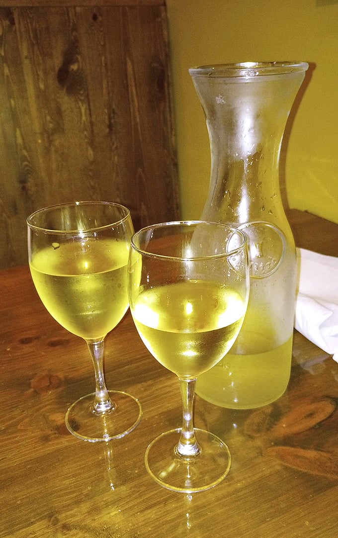 A carafe of house white wine catches the light like liquid sunshine—the perfect companion for Mediterranean flavors and leisurely conversation.