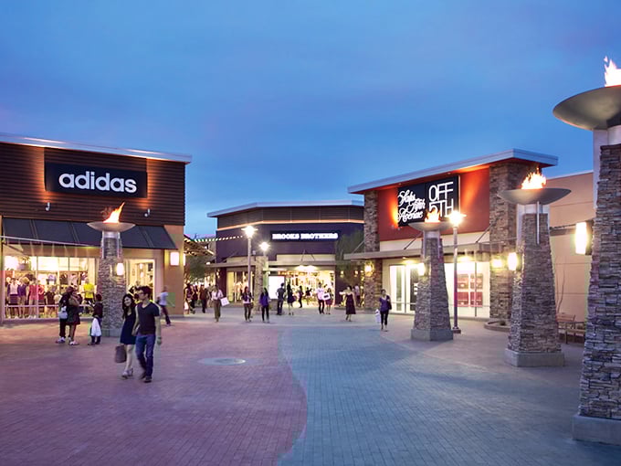 As twilight falls, the outlet mall transforms into a glowing wonderland where credit cards practically swipe themselves.