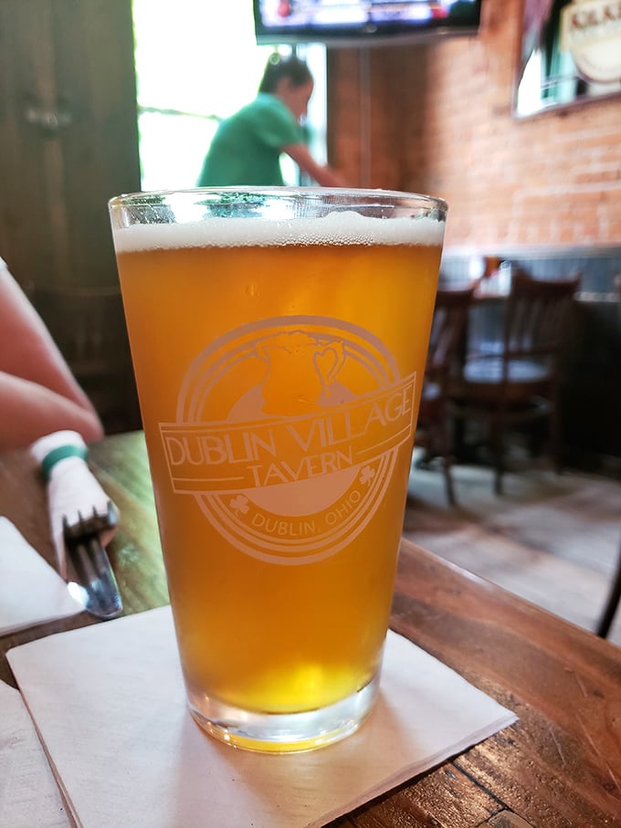 A perfectly poured pint catches the light, its amber glow and foamy head promising refreshment with the tavern's logo as a seal of quality.