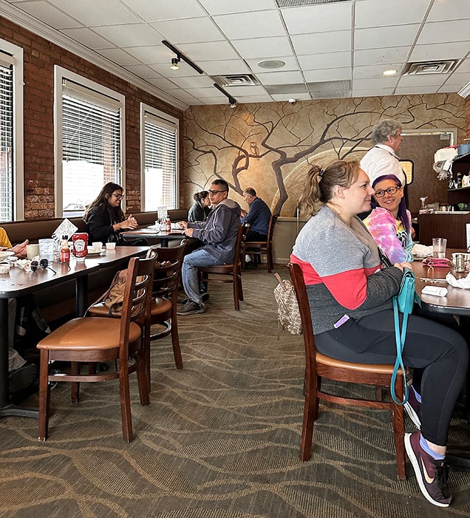 The dining room hums with conversation and clinking silverware against a backdrop of warm wood tones and an artistic tree mural.
