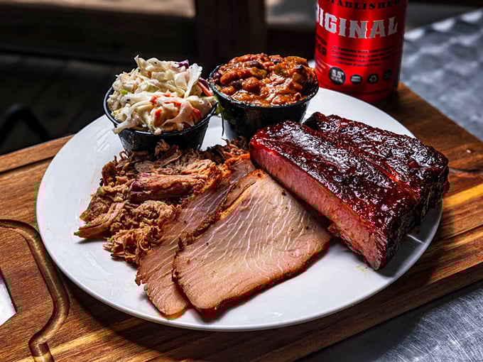 The carnivore's dream team – brisket, pulled pork, and ribs sharing a plate with coleslaw and baked beans. This wooden board holds the barbecue trifecta.
