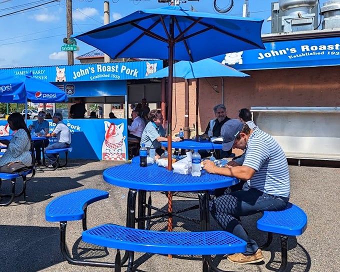 The outdoor seating area proves good things come to those who wait—blue umbrellas, picnic tables, and the promise of sandwich nirvana just steps away.