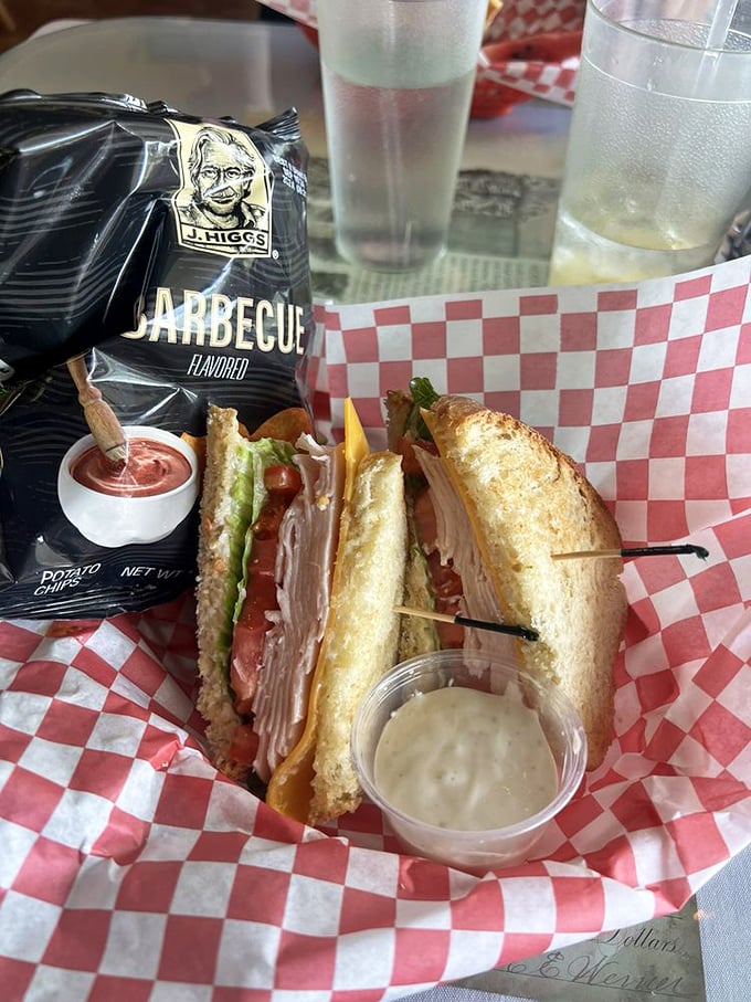 A sandwich so perfectly constructed it deserves architectural recognition, served with chips and that essential pickle spear for proper lunch balance. 