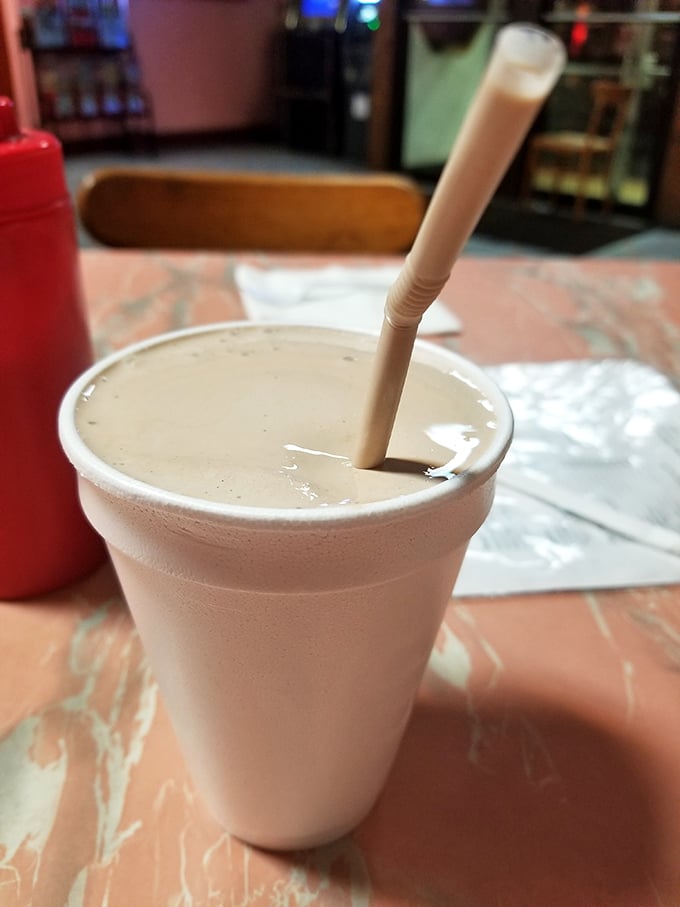 The milkshake arrives in its natural habitat—a styrofoam cup with a straw standing at attention, promising cool, creamy relief between bites of savory perfection.