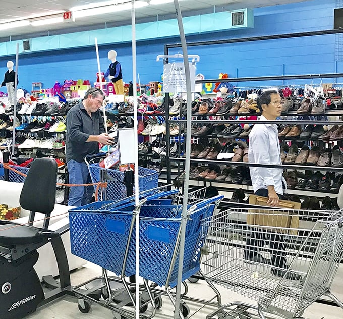 Thrift store anthropology in action—shoppers navigate the shoe section with the focus of archaeologists uncovering treasures from the recent past.