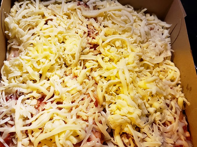 A blanket of unmelted cheese awaits its destiny in the oven. Anticipation is half the pleasure of Police Station Pizza.