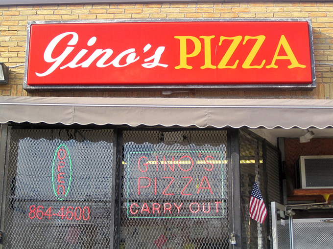 Gino's bold red sign pops against the yellow brick building. Those security screens protect pizza worth breaking in for!