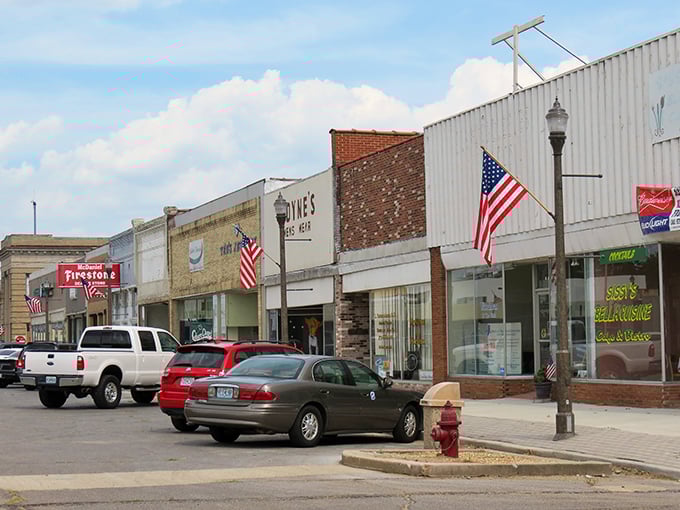 American flags flutter proudly along the street where local businesses still remember your name and preferences.