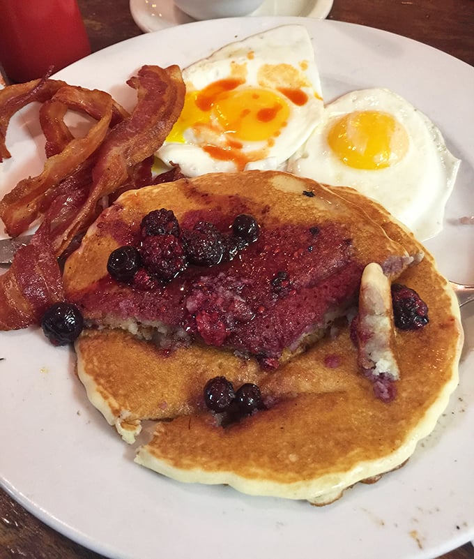 Blueberry pancakes sharing plate space with perfectly cooked eggs and bacon – breakfast's greatest hits album on a single white plate.
