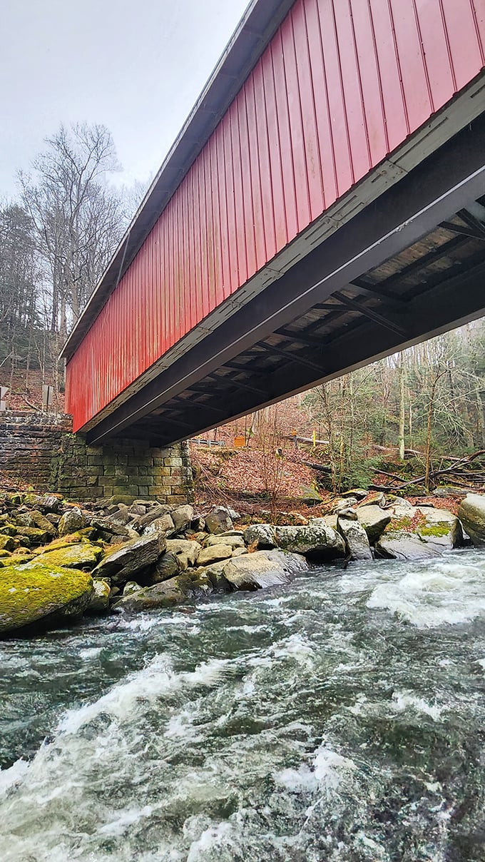 From below, the bridge reveals its engineering secrets – massive stone abutments supporting the wooden structure while Slippery Rock Creek dances over ancient boulders.