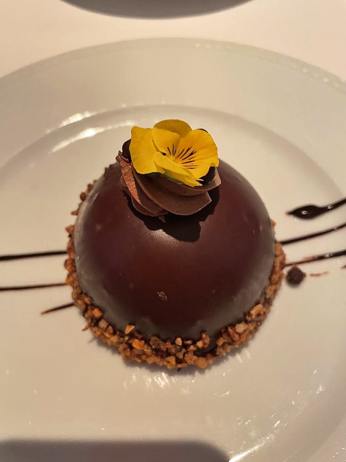 The chocolate dome dessert wears its edible flower like a tiny hat at the Kentucky Derby—elegant, whimsical, and destined for Instagram fame.