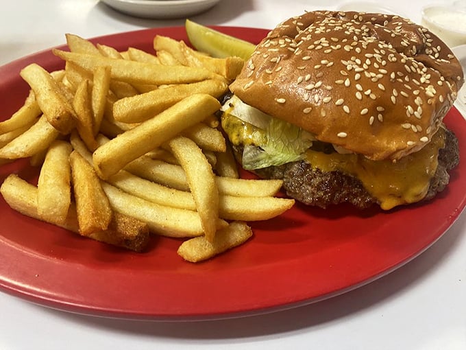 The cheeseburger in its natural habitat—surrounded by golden fries on a red plate. A timeless American romance.