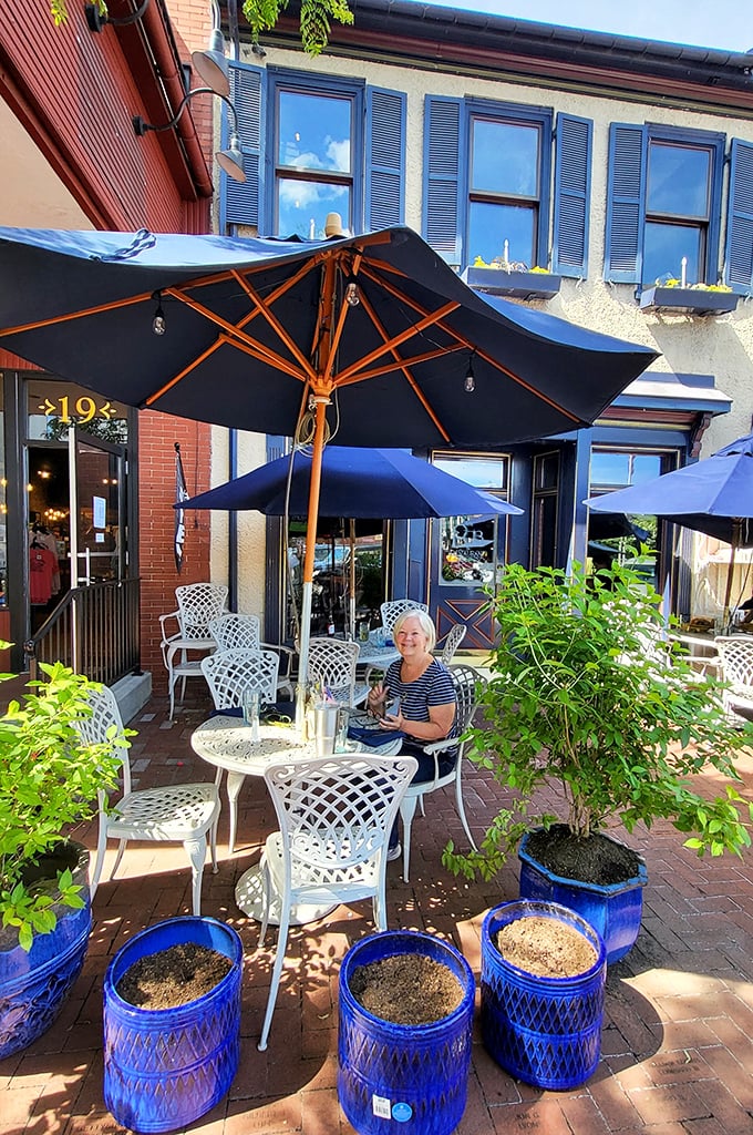 The outdoor seating area, framed by blue planters and dappled sunlight, creates the perfect stage for people-watching between bites.