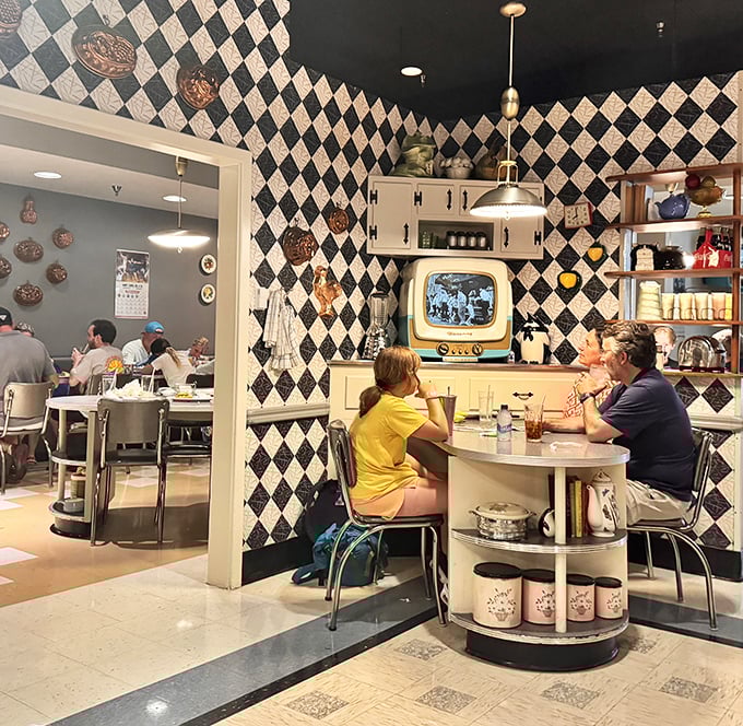 Families gather around kitchen tables while vintage TVs flicker with black-and-white memories. The checkered walls aren't the only things with patterns—so is the conversation.