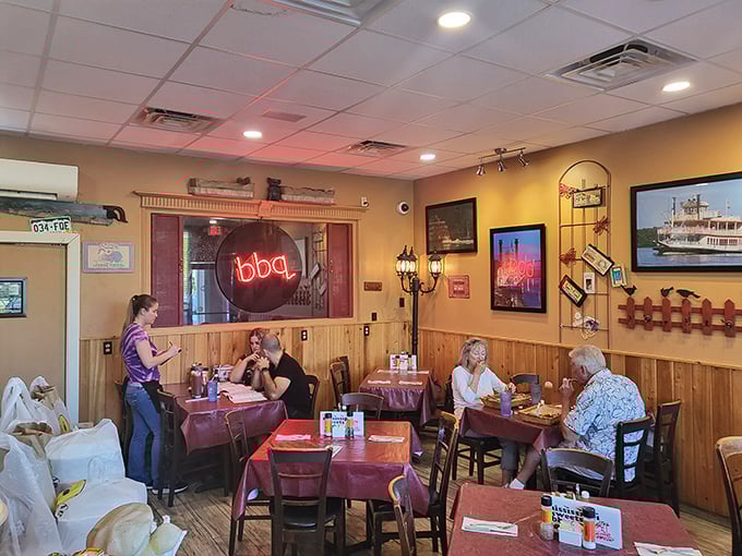 The neon BBQ sign glows like a beacon for hungry souls, while burgundy tablecloths add a touch of unexpected elegance.