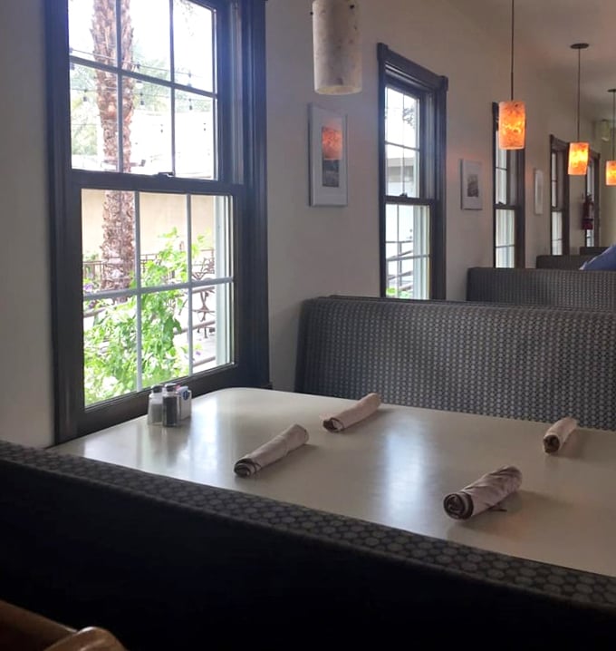 Sunlight streams through windows framing palm trees outside, while amber pendant lights create the perfect ambiance for desert dining.
