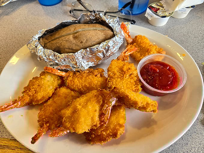 Jumbo fried shrimp stand at attention next to a foil-wrapped baked potato. This plate says "I'm treating myself" without saying a word.