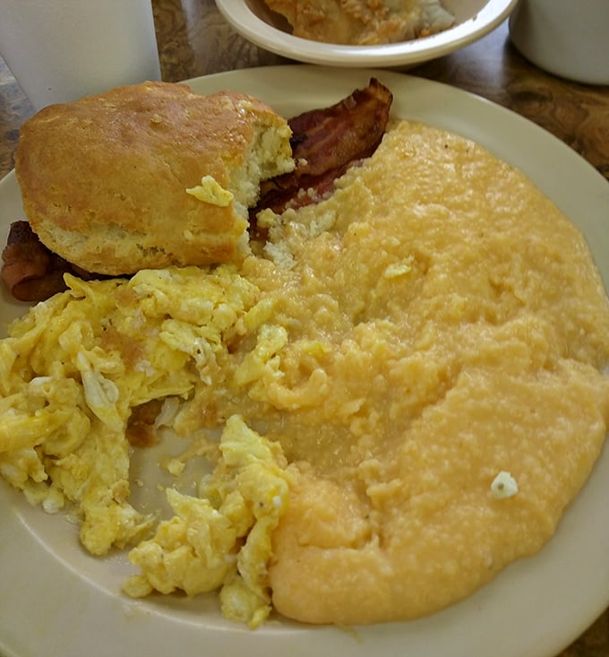 The breakfast trinity: eggs, grits, and bacon with a biscuit standing by – morning salvation on a simple white plate.