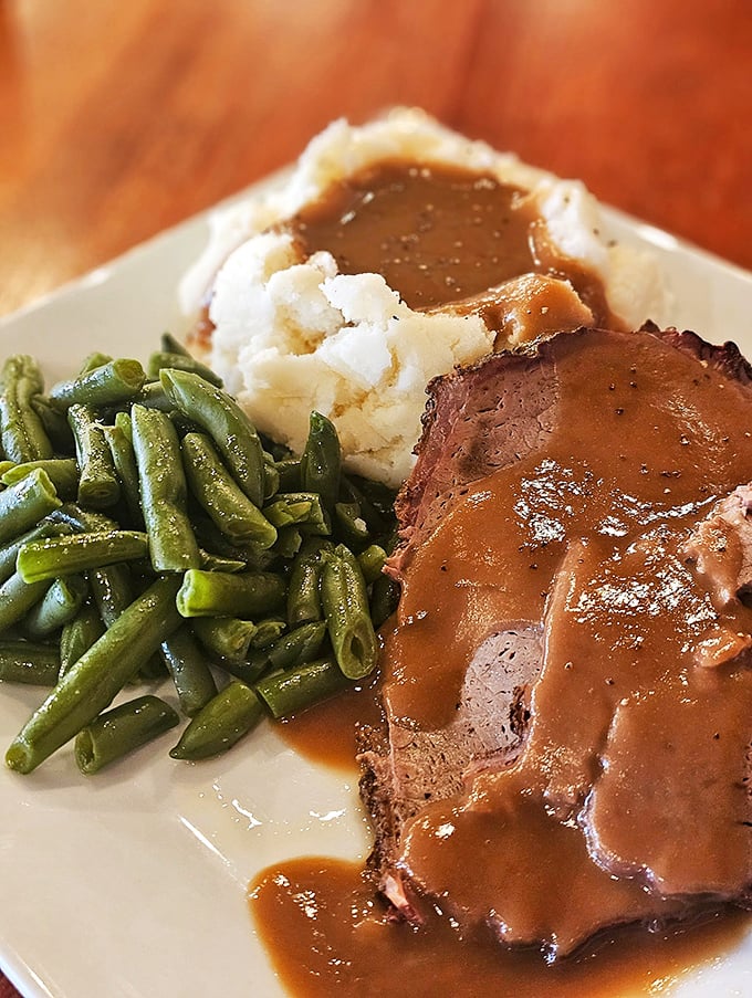 A plate that understands the importance of gravy lakes touching every island of food. Those green beans are just pretending to be healthy—they've been partying with pork all day.