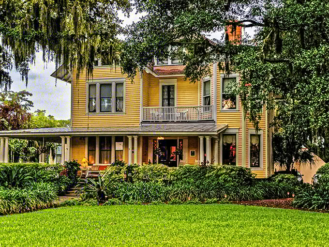 Sunshine yellow Victorian charm wrapped in Spanish moss and tropical foliage—the kind of porch that practically demands a good book and glass of sweet tea.