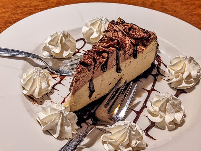 This isn't just cheesecake—it's a chocolate-drizzled masterpiece surrounded by whipped cream sentinels standing guard until your fork arrives.