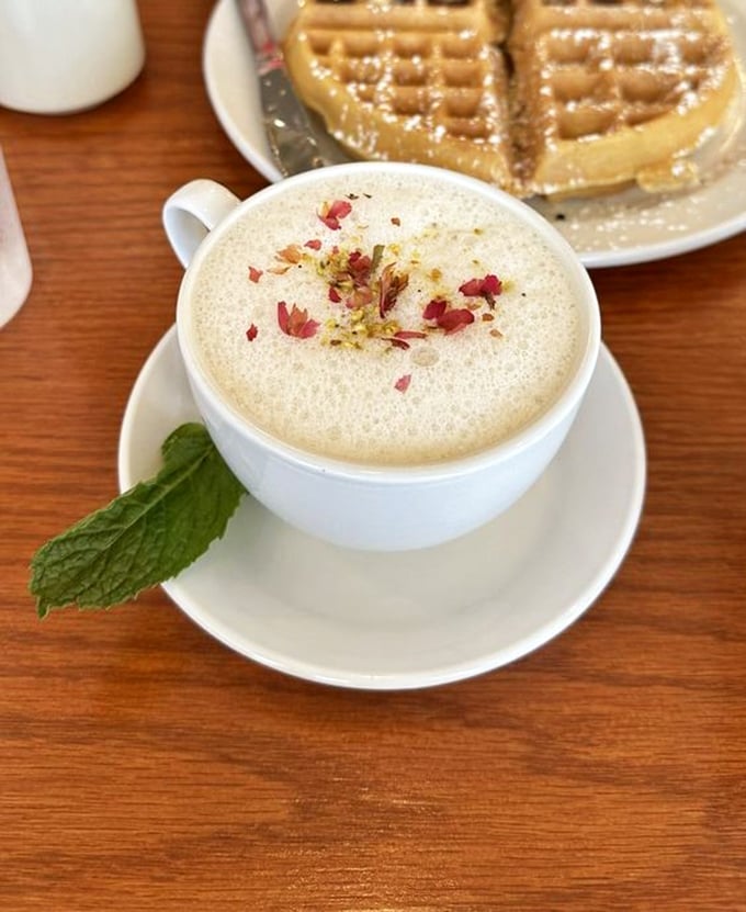 A pistachio rose latte that's dressed better than most people at brunch, topped with delicate petals and paired with golden waffles.