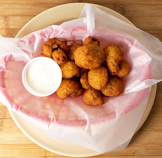 These golden hush puppies aren't just fried—they're little orbs of cornmeal joy that somehow taste like childhood and comfort all at once.