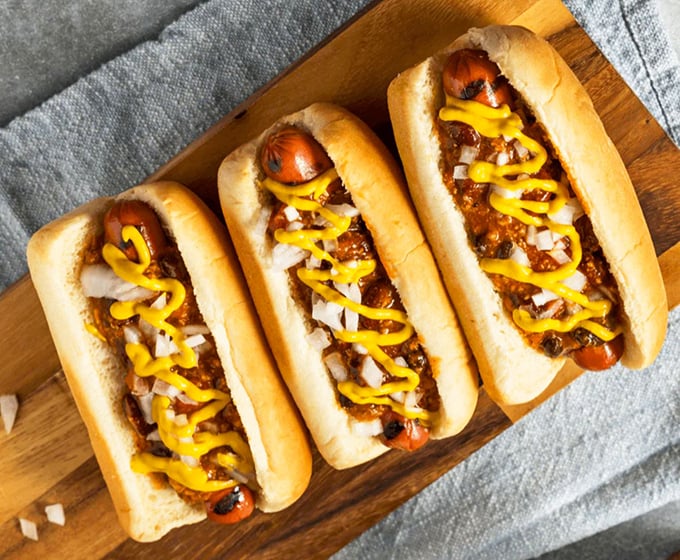 Three chili dogs lined up like soldiers ready for duty. The mustard zigzag isn't decoration—it's the yellow brick road to flavor town.