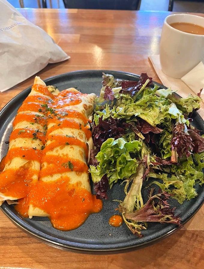 Savory crepes draped in vibrant sauce alongside fresh greens—proof that breakfast can be both sophisticated and deeply satisfying.