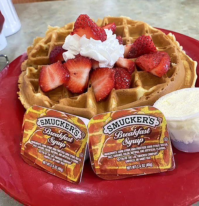 A golden waffle crowned with fresh strawberries and whipped cream—breakfast that boldly crosses into dessert territory without apology.