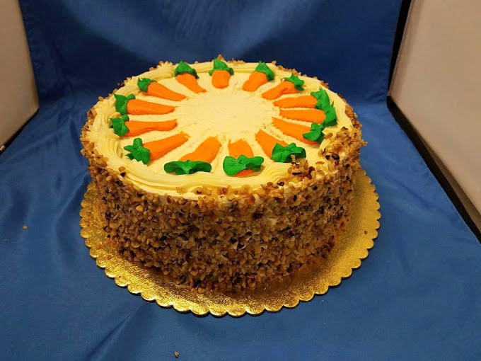 This carrot cake wears its cream cheese frosting like a crown. Those decorative carrots aren't fooling anyone—this is dessert, gloriously unapologetic.