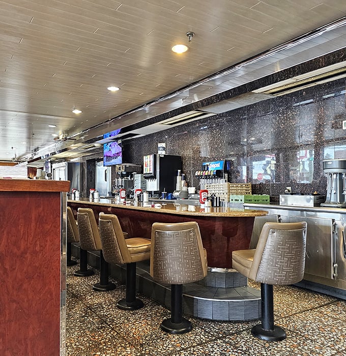 The counter seating—where solo diners become regulars, and the coffee refills flow as freely as the conversation with your favorite server.